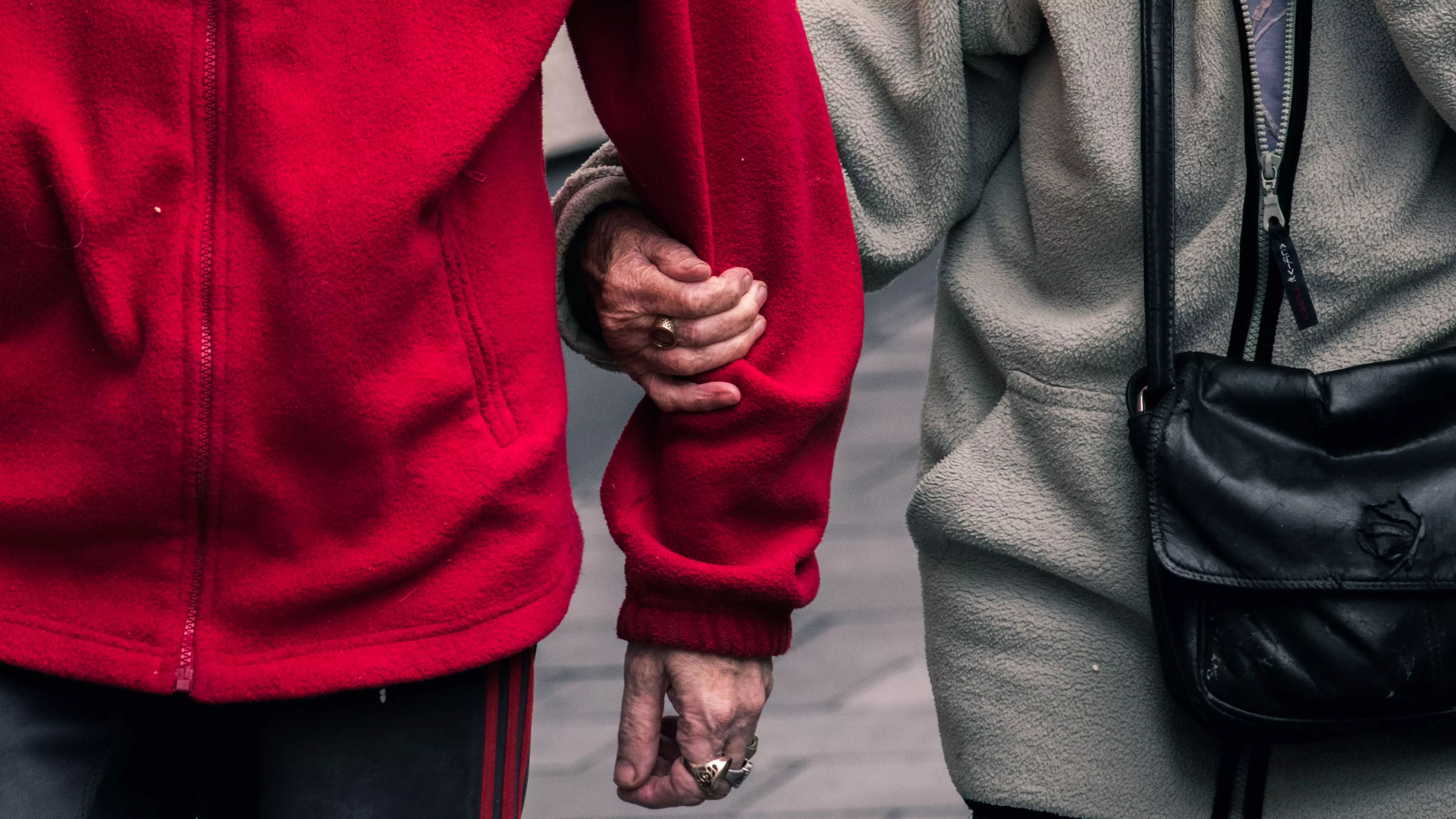 Двама по-възрастни възрастни се държат за ръце, докато вървят.