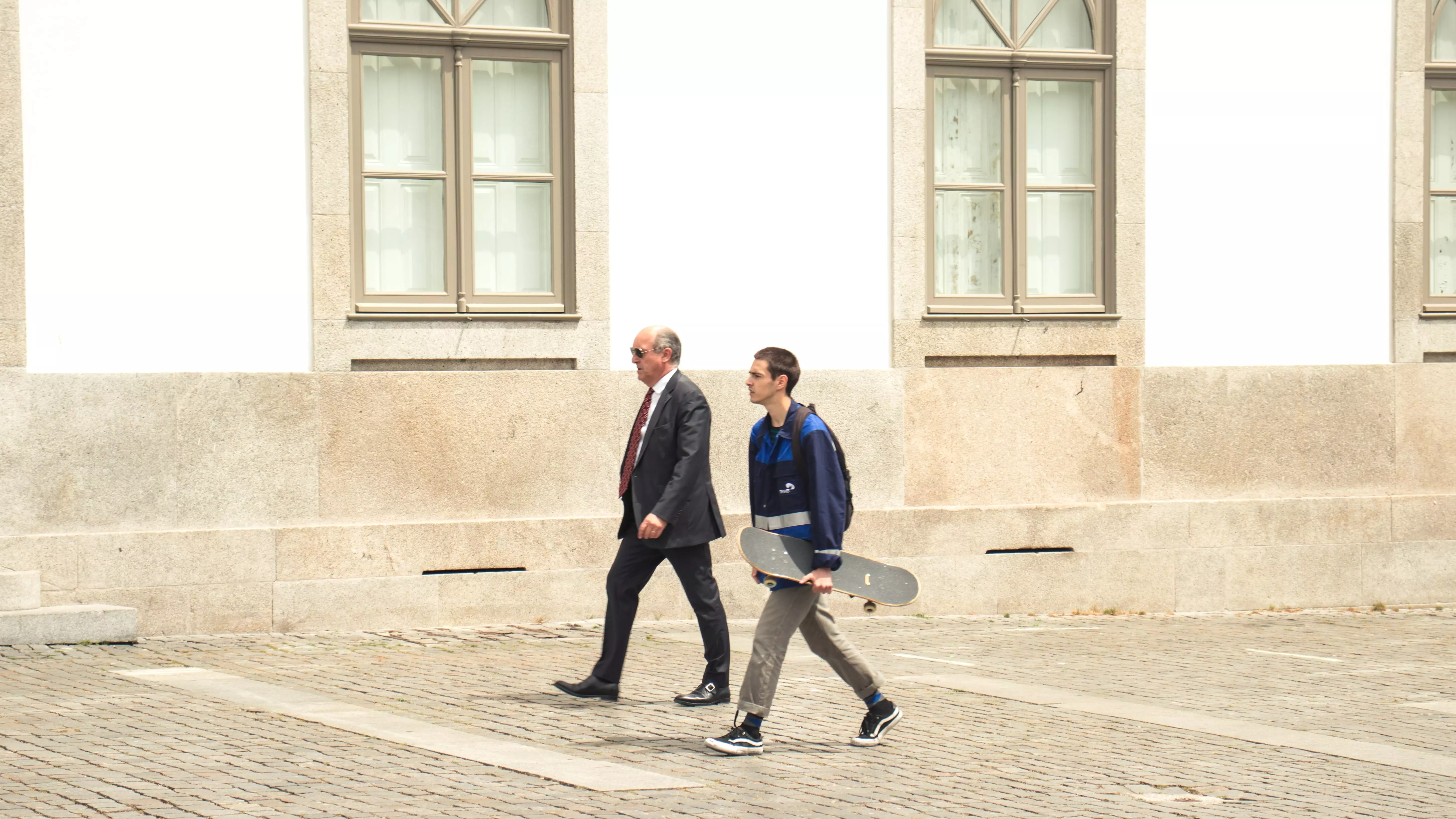 Կոստյումով տղամարդը քայլում է սքեյթբորդ կրող դեռահաս տղայի կողքով՝ պատկերելով կյանքի փուլերը: